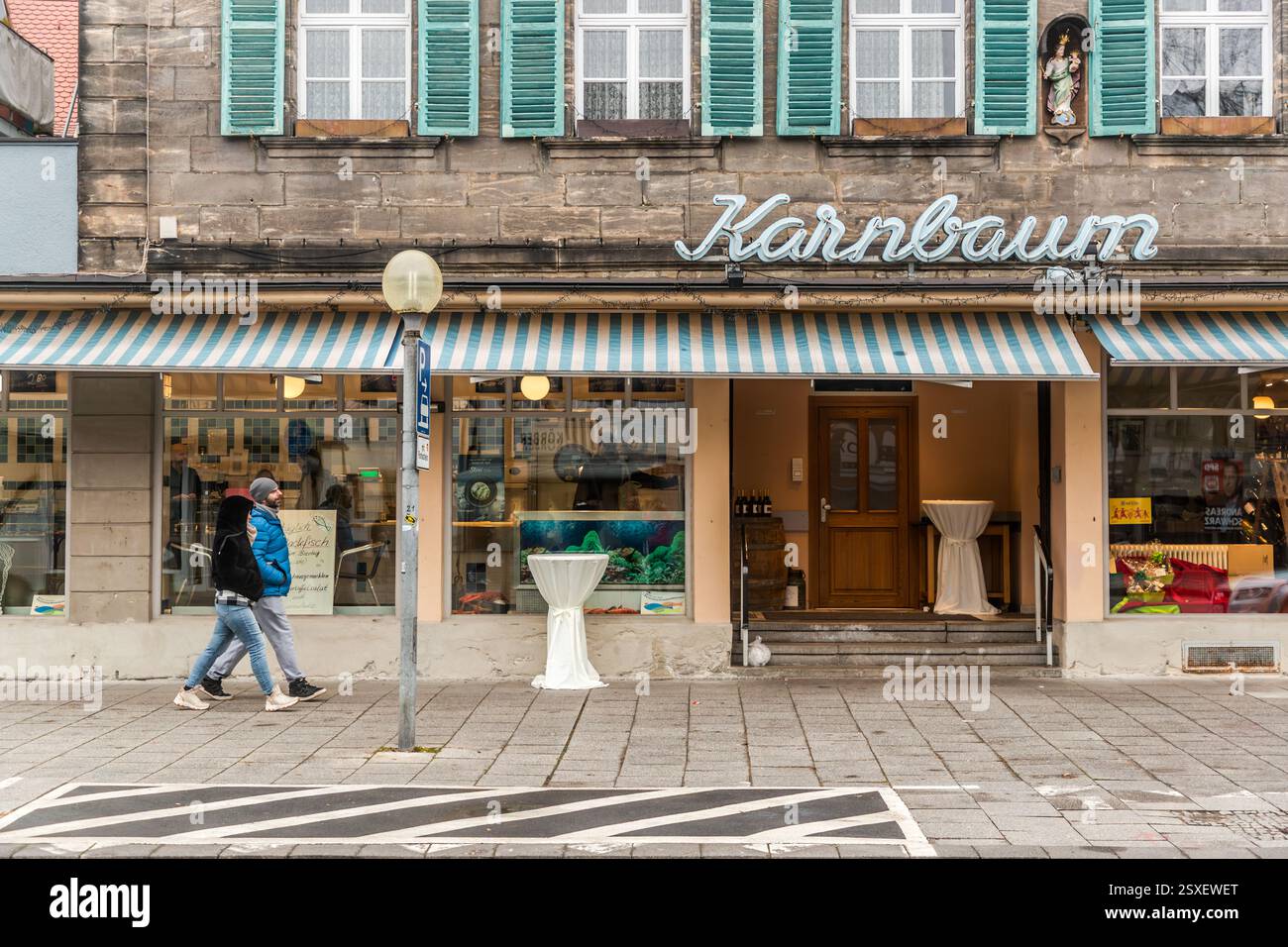 Pedestrians walk past a fish shop in Germany called Karnbaum. A couple ...