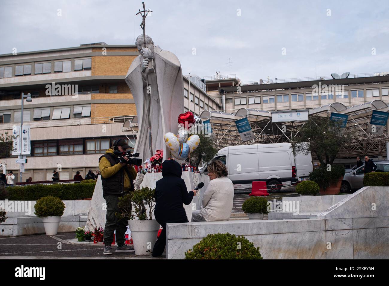 A TV crew interviews a faithful person praying under the statue of Pope ...