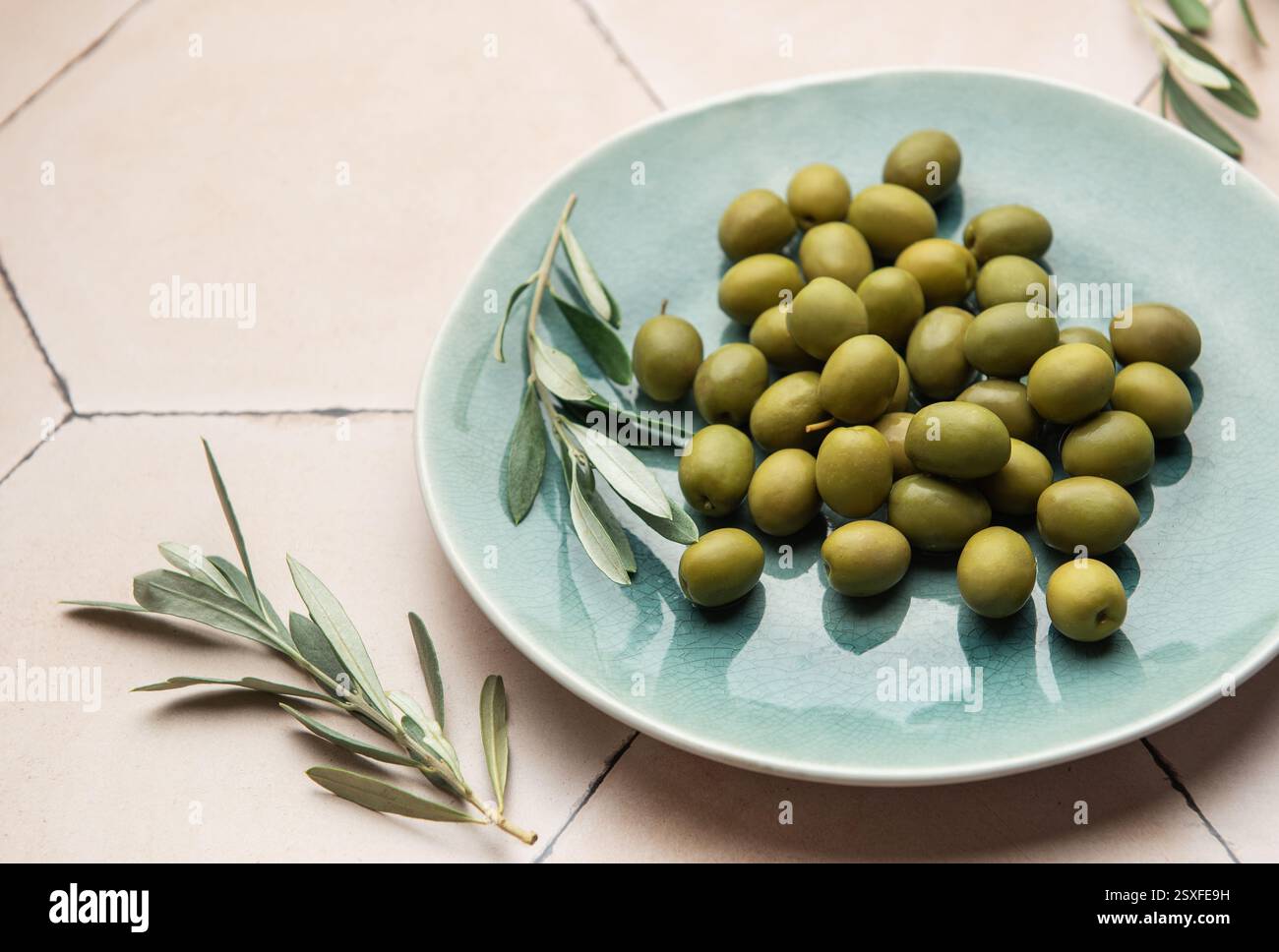 Green olives arranged on a ceramic plate, garnished with a fresh olive ...