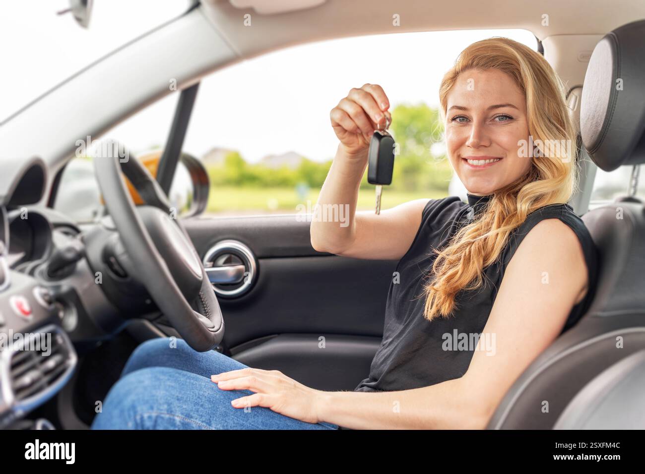 A smiling blonde woman sits in the drivers seat of a modern car ...