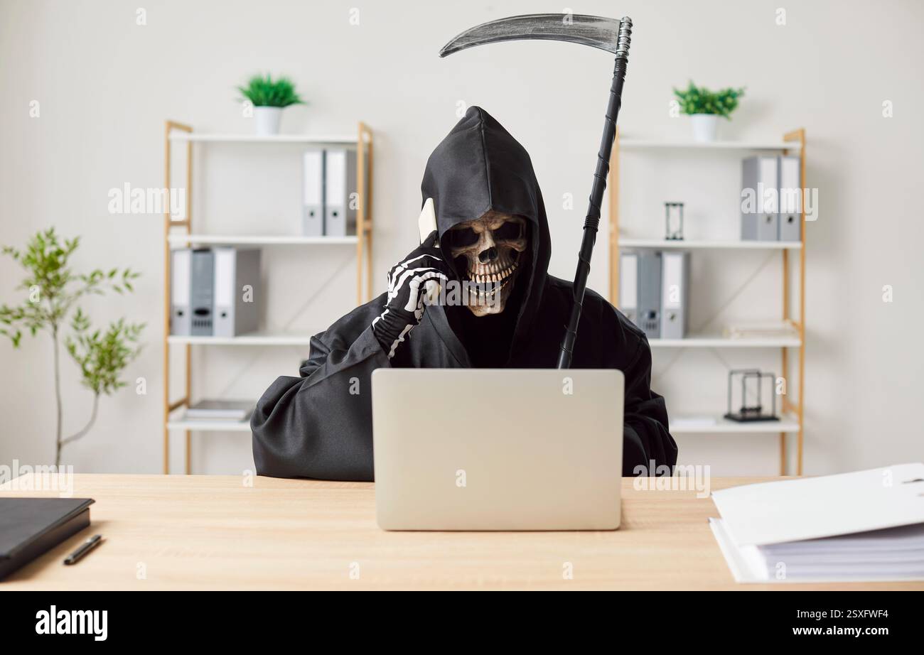 Funny man wearing black death suit with skull mask works while sitting ...