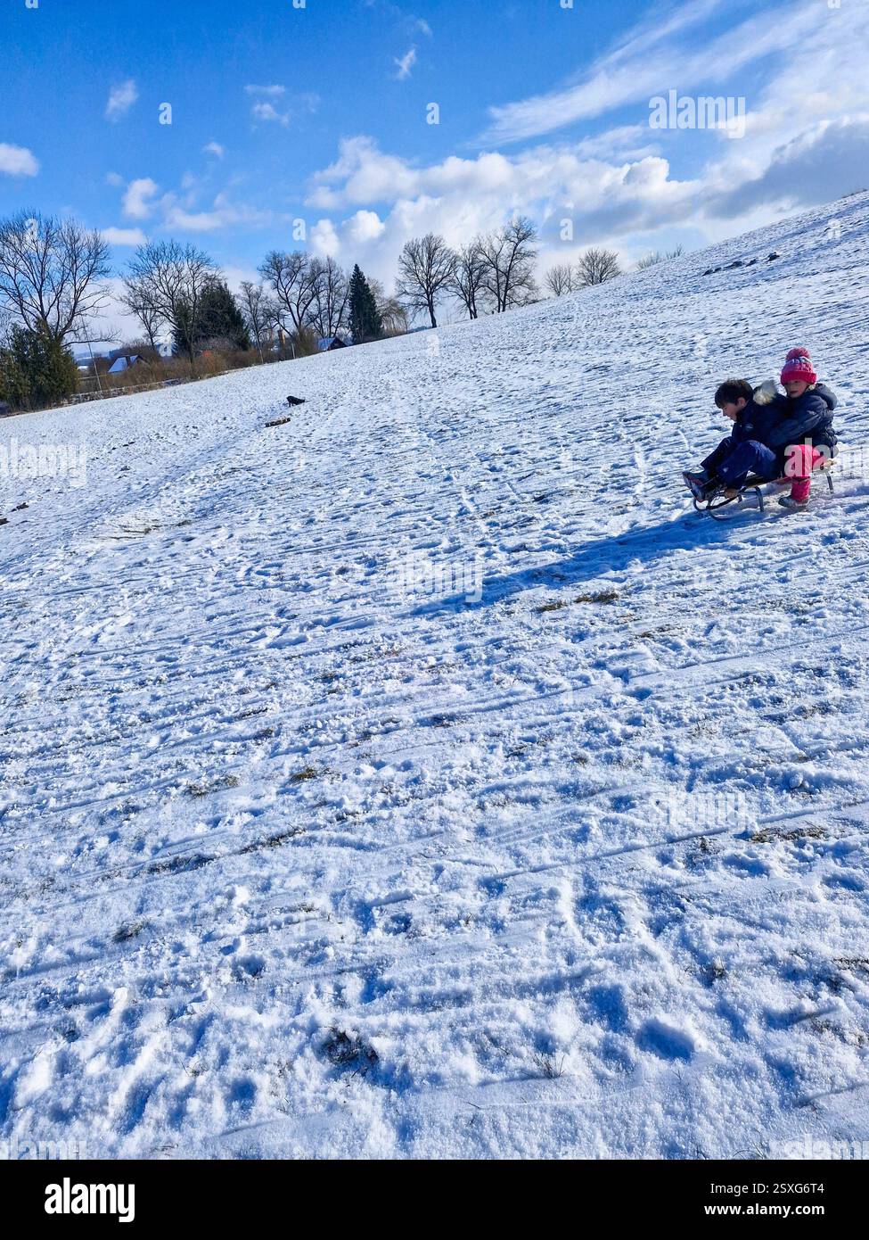 Two children on small sleds are sliding down a steep snowy hill Stock ...