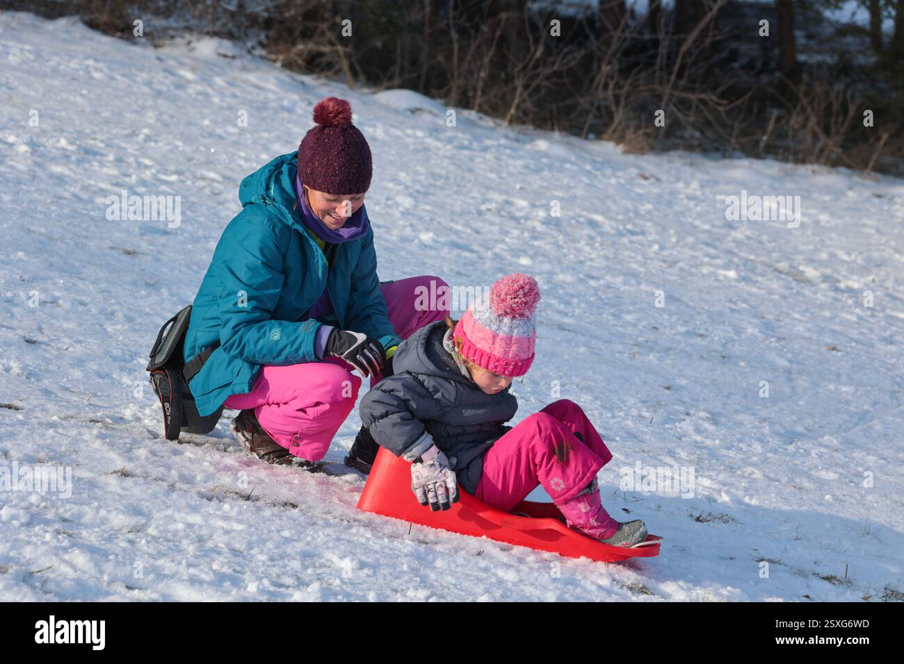 Mom helps daughter get on bobsleigh while sledding in the snow Stock ...