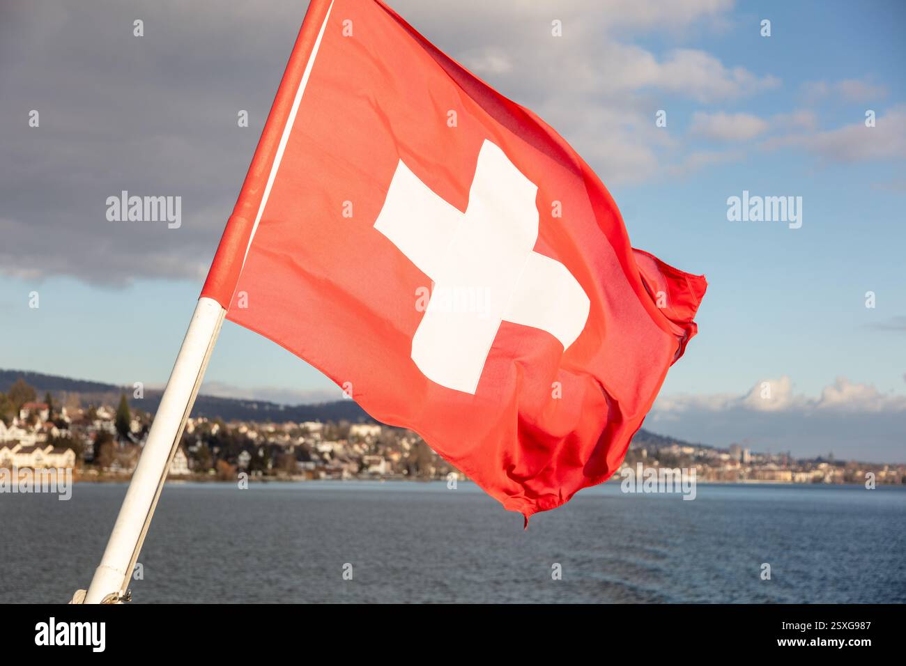 Swiss flag waving in the wind mounted on a ferry, Lake coast with ...