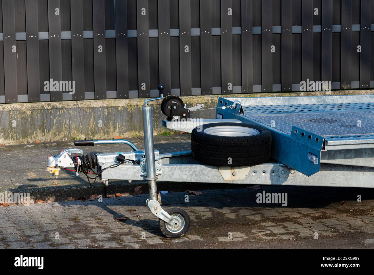A utility trailer is positioned on a paved surface, featuring a single ...