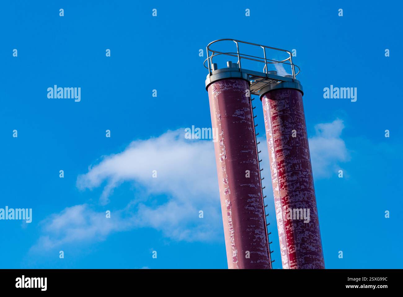 Two tall, weathered chimneys stand prominently against a bright blue sky. The structures show ...