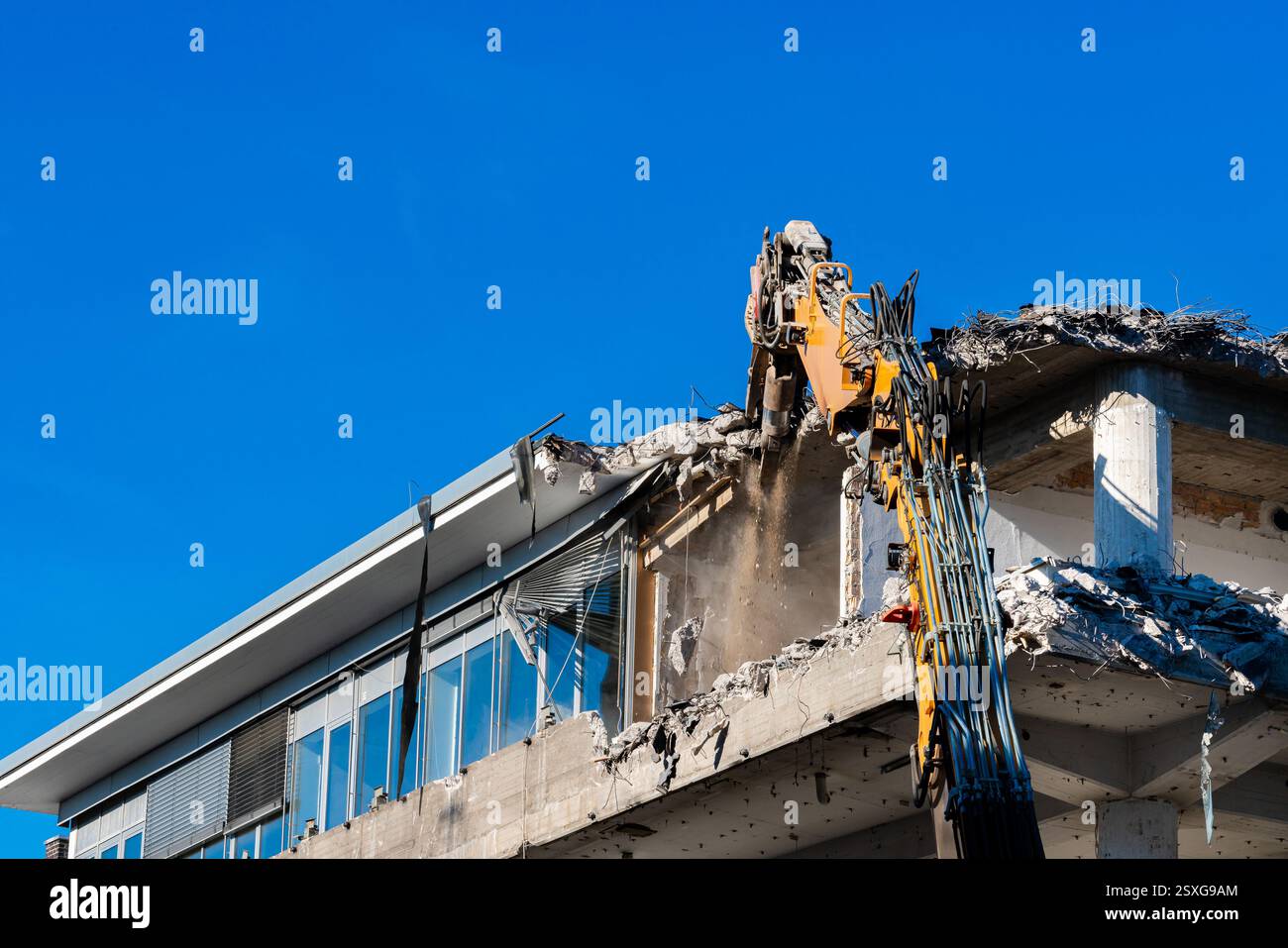 Heavy machinery is actively demolishing a multi-story building. Dust and debris fill the air as ...