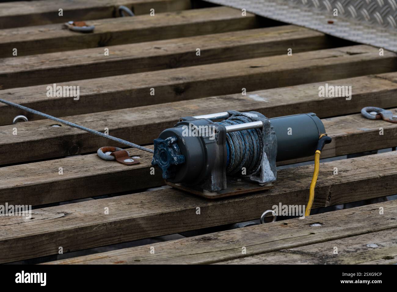 A winch is stationed on a weathered wooden car trailer. The setup ...