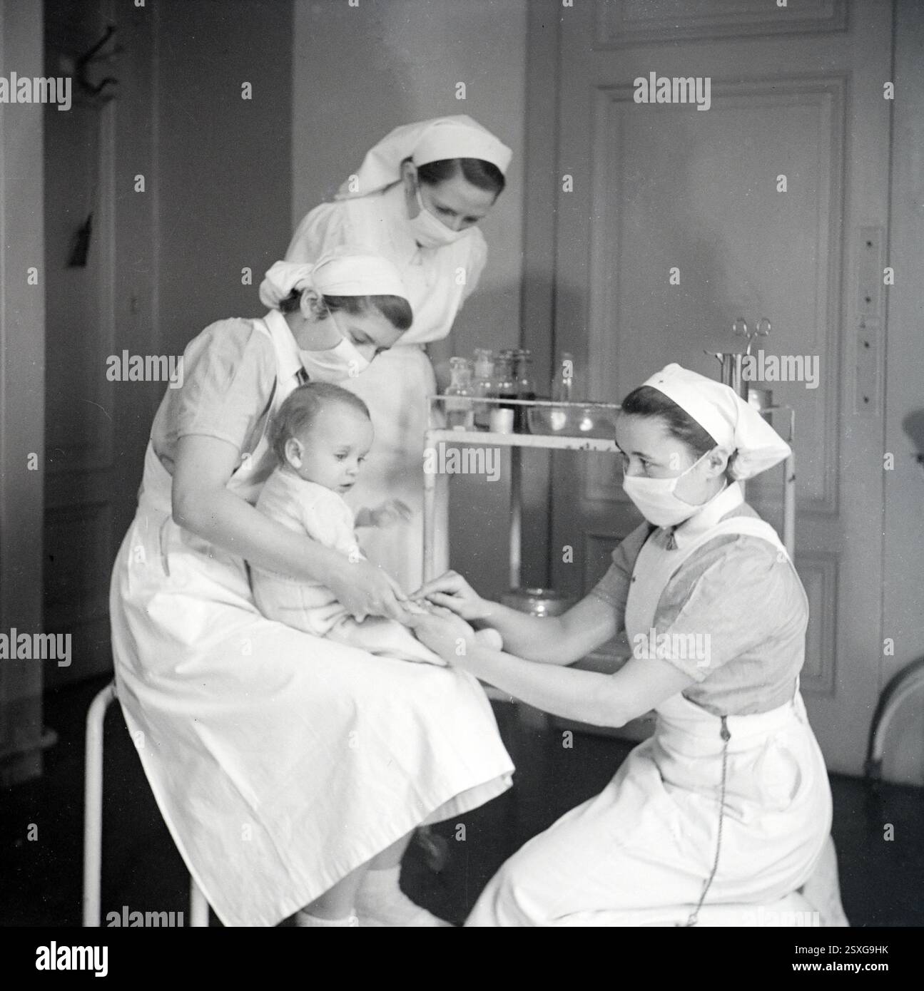 Three Red Cross Nurses Wearing Medical Masks Looking After Baby in ...