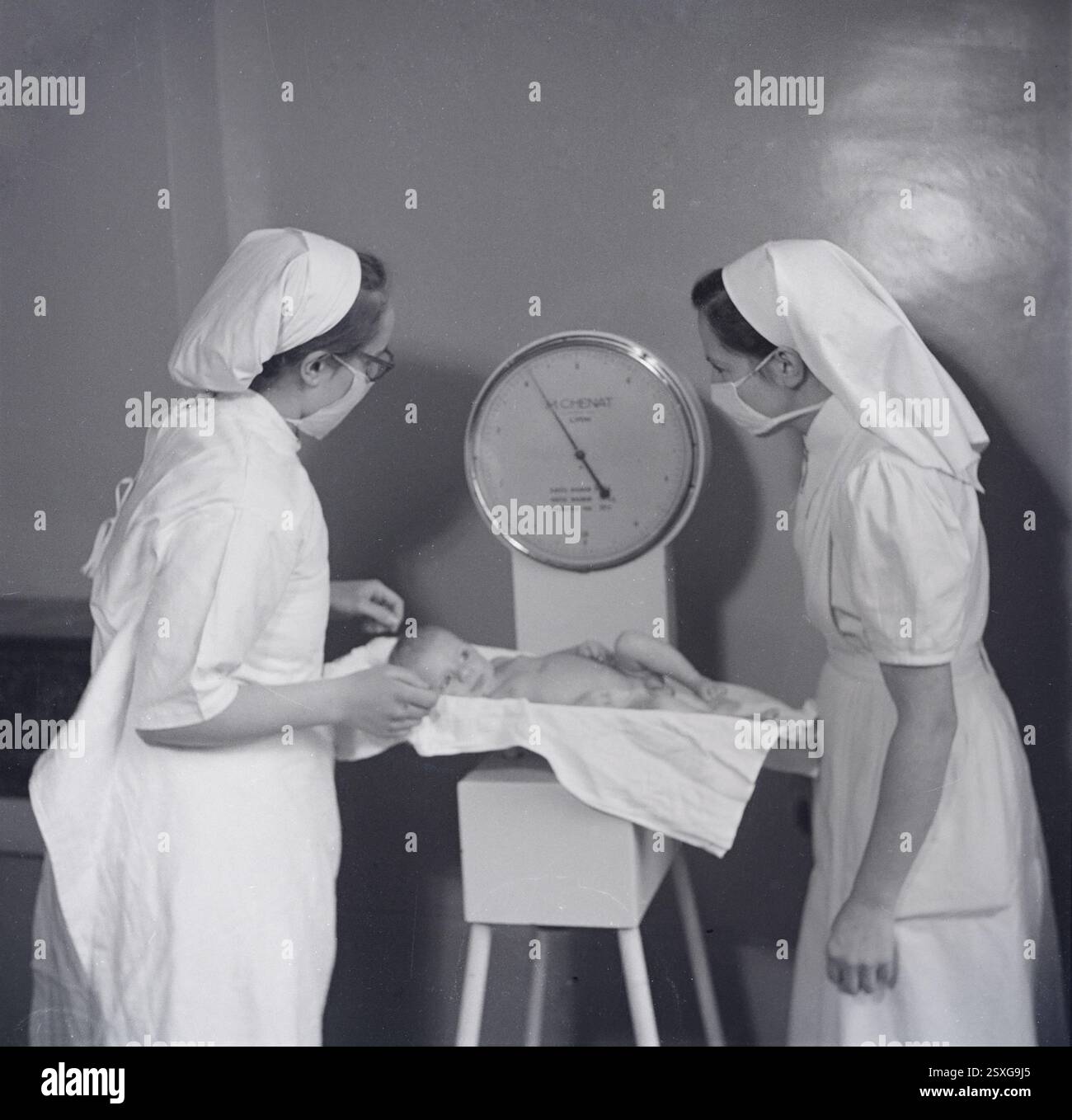 Two Red Cross Nurses Wearing Medical Masks Weighing Baby in Materinity ...