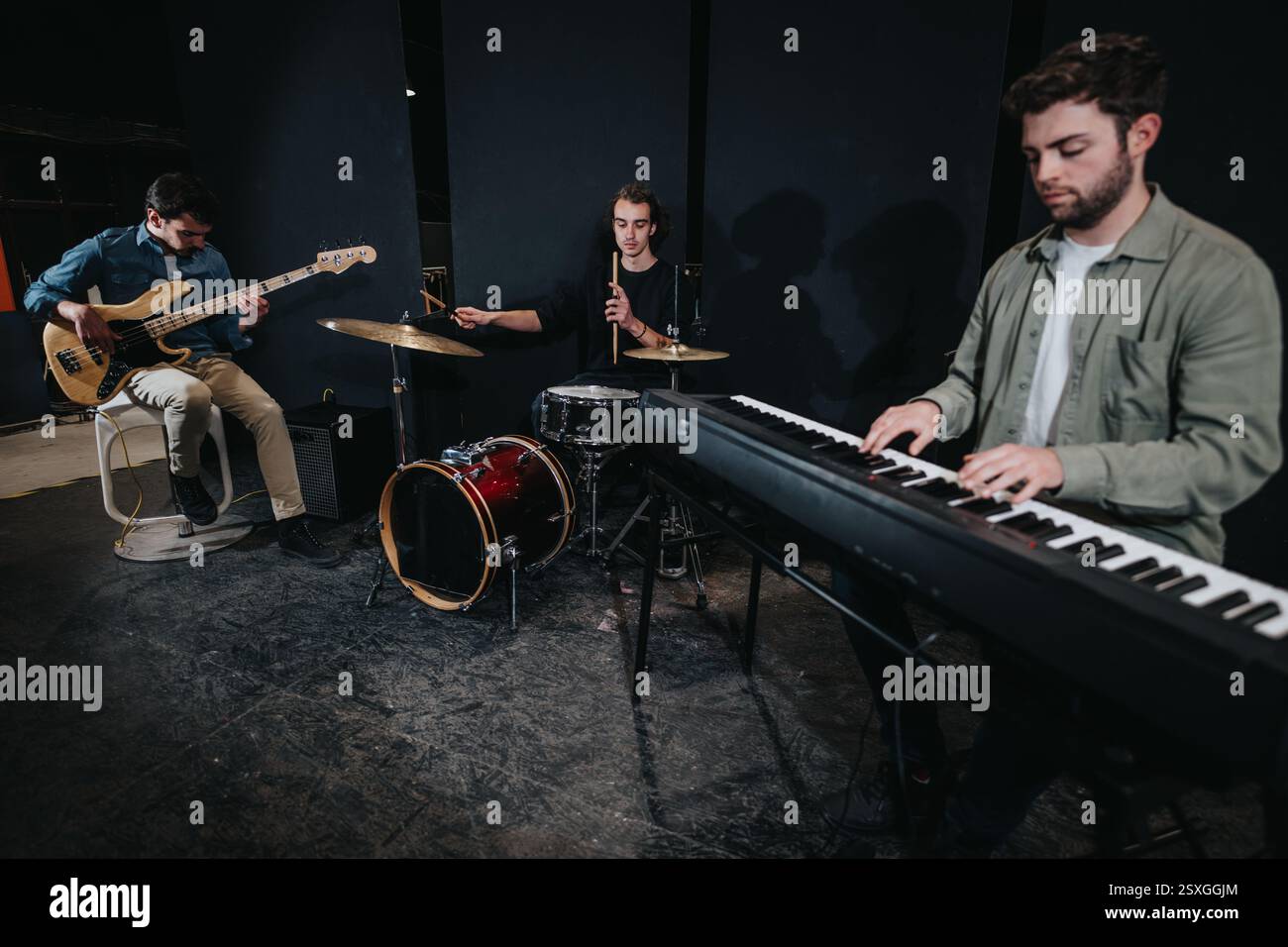 Three musicians rehearsing together with keyboard, drums and guitar ...