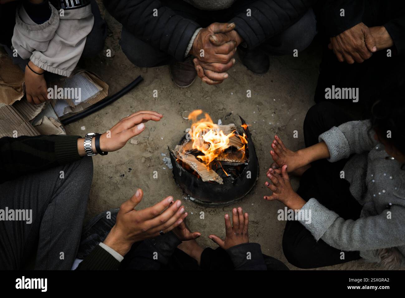 Members of Abed family, warm up by a fire at a tent camp for displaced ...