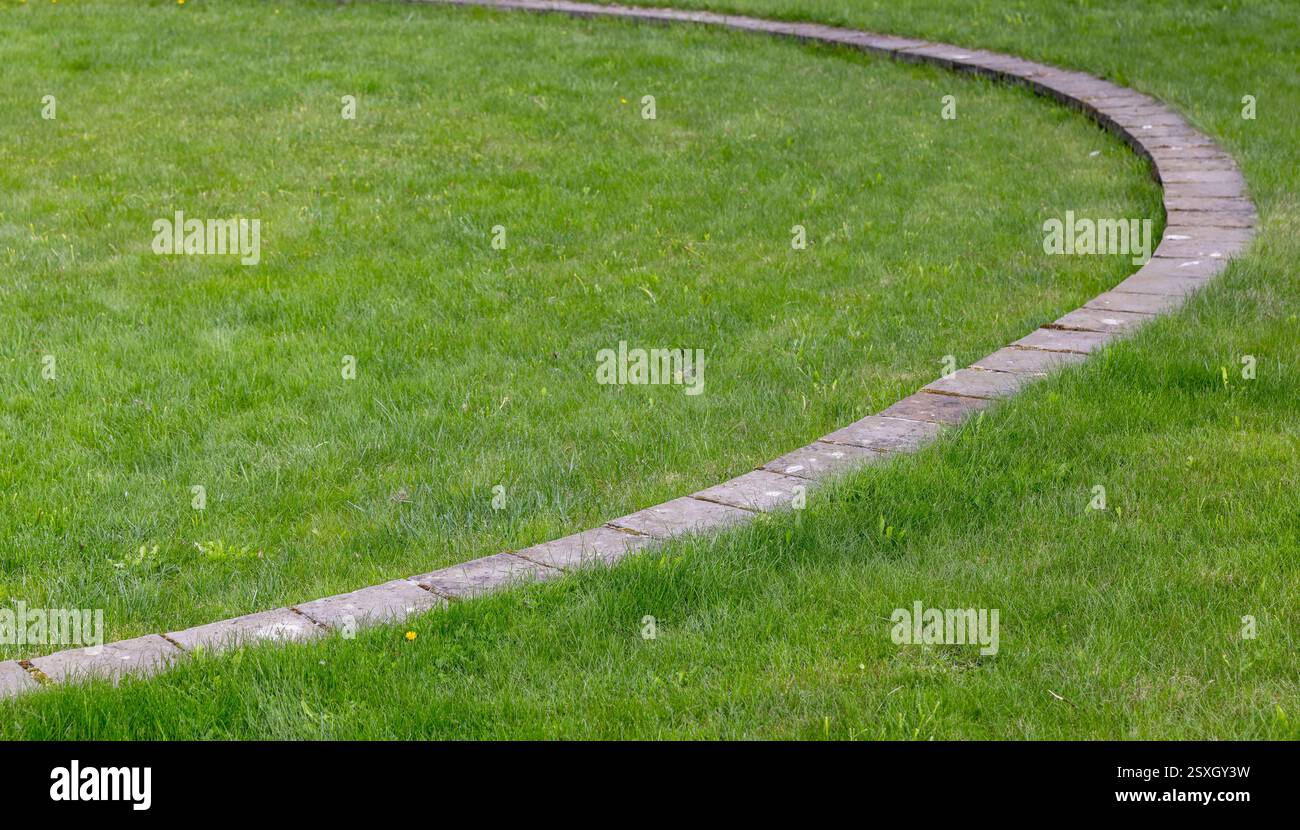 A well-maintained brick pathway curves through a vibrant green lawn ...