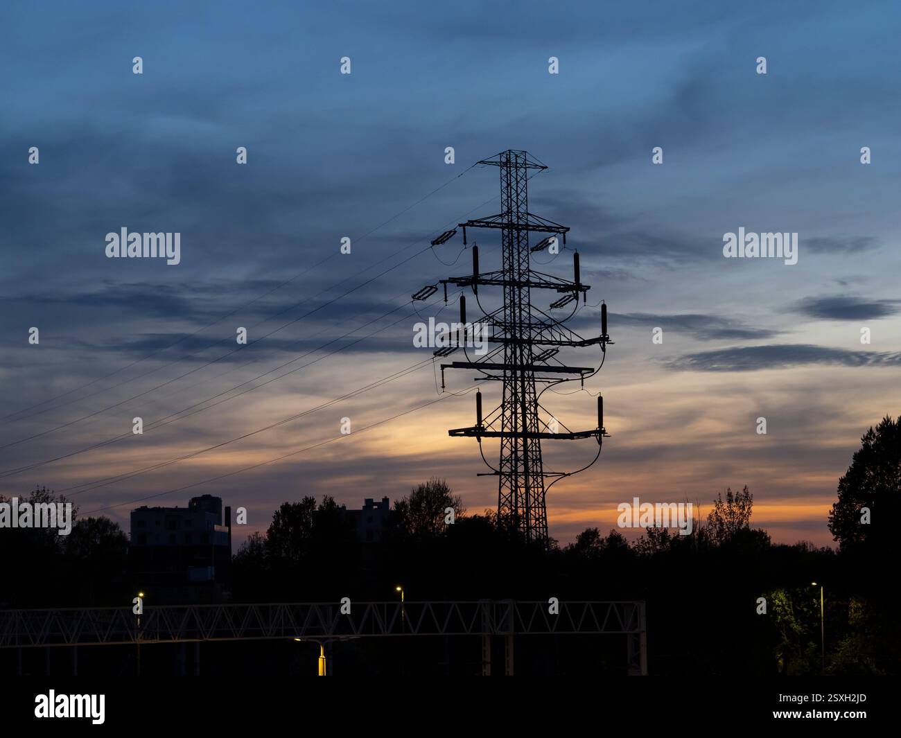 Electricity transmission tower silhouetted against a vivid sunset, showcasing energy ...
