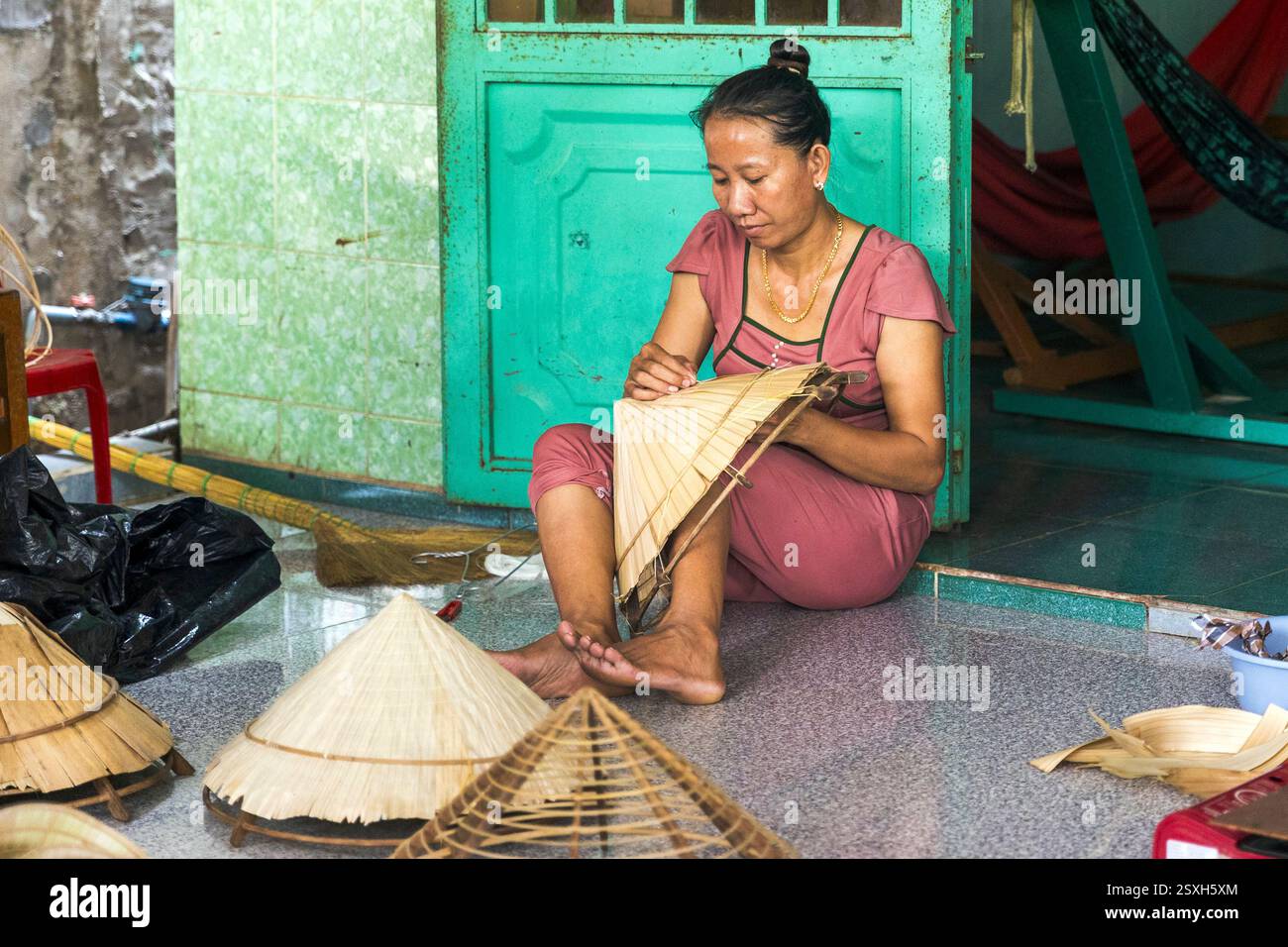 A woman engaged in traditional craft work making bamboo conical hats ...