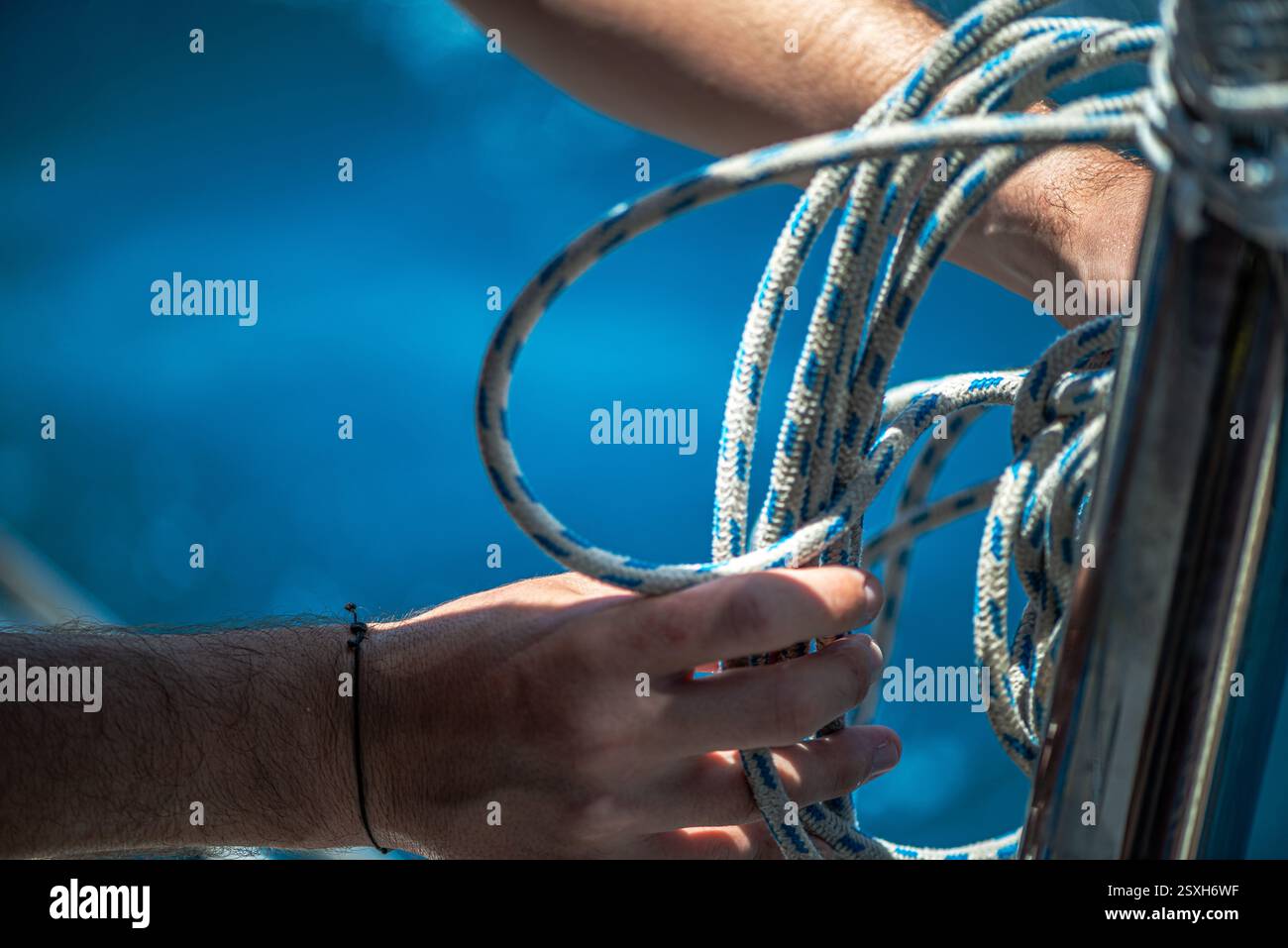 A close-up view of hands tying a strong knot with a ship rope on a sail ...