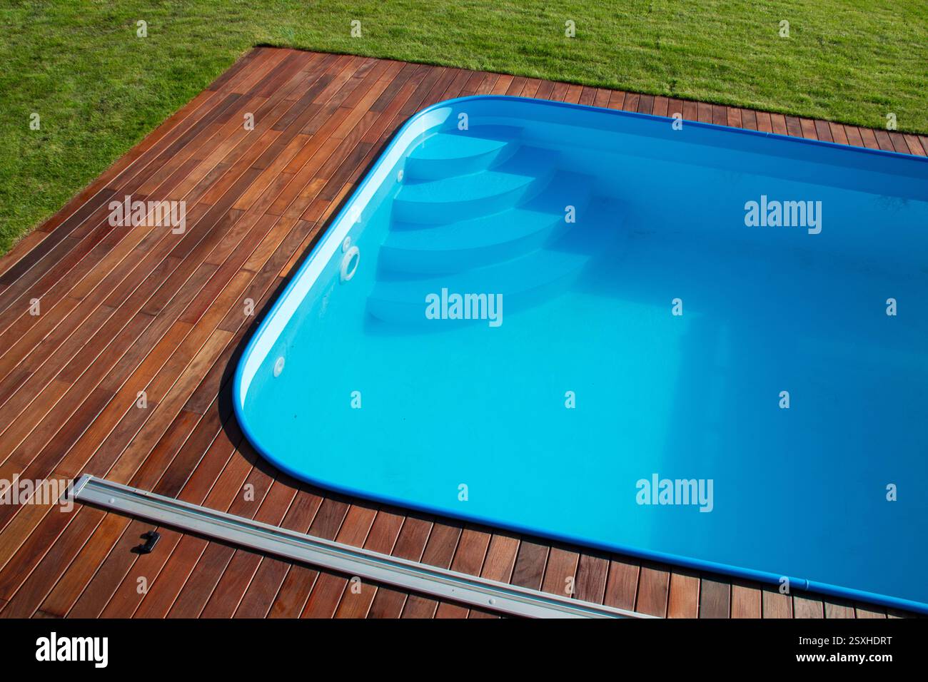 A clean, bright blue swimming pool is featured with steps leading down ...