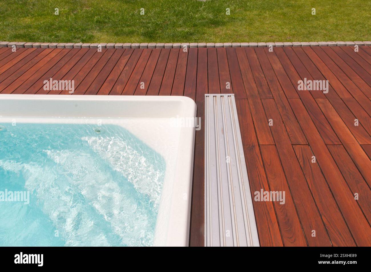 A beautiful wooden deck encircles a clear swimming pool, reflecting ...
