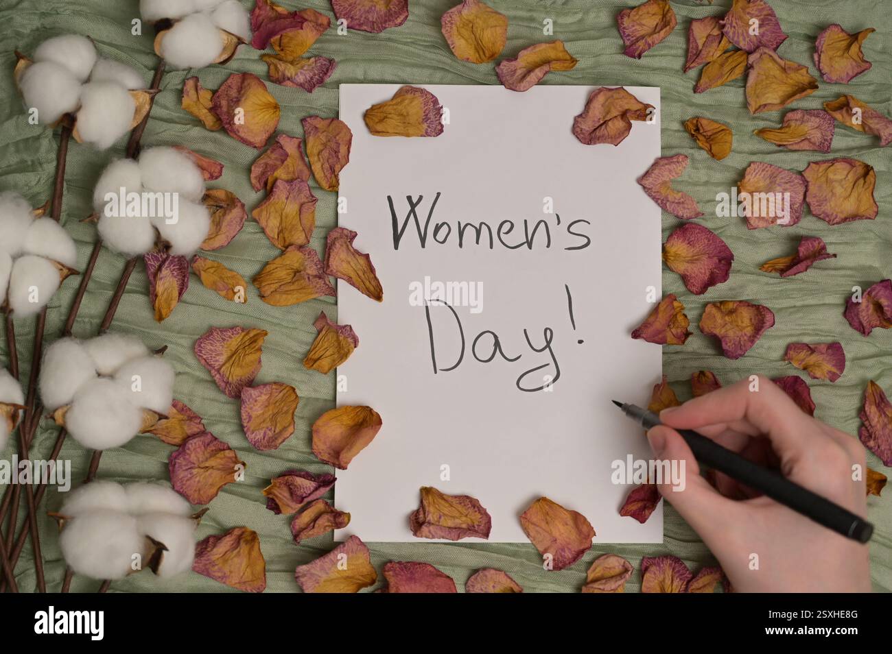 Woman's hand with a pen writing "Women's Day!" on white paper. Green ...