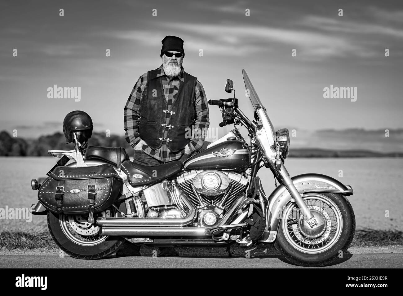 Rocker - kultig aussehender Motorradfahrer steht hinter seiner Harley ...