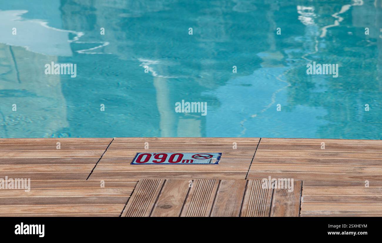 Wooden deck with a depth marker beside a clear blue swimming pool ...