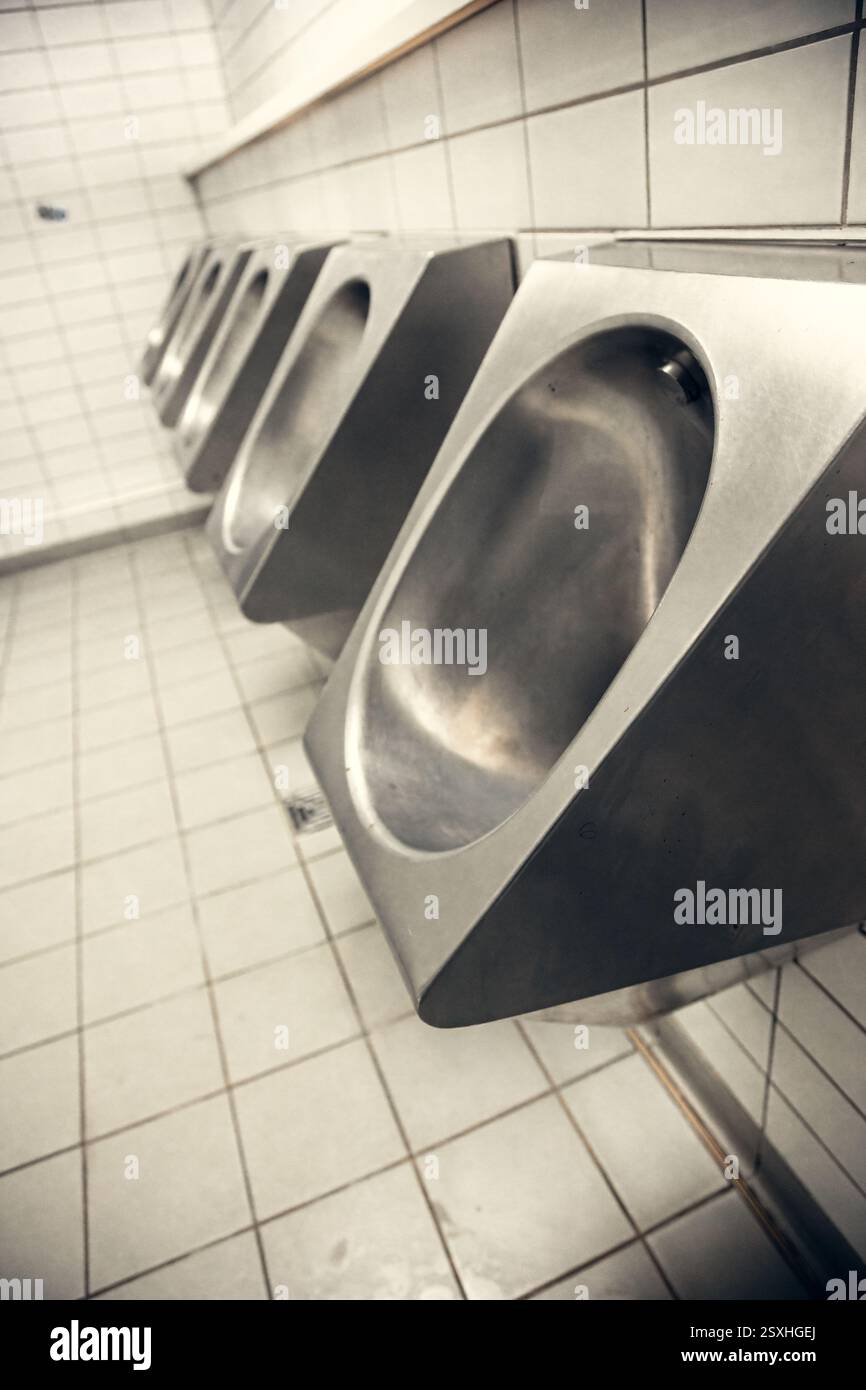 A row of stainless steel urinals in a public restroom with white tiled ...