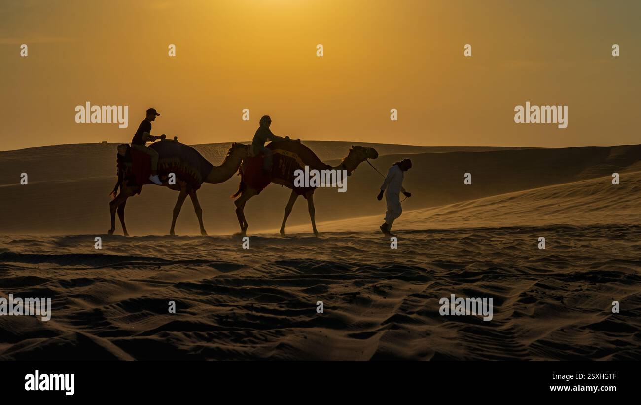 Doha, Qatar, February 24, 2025: A group of people riding camels through ...