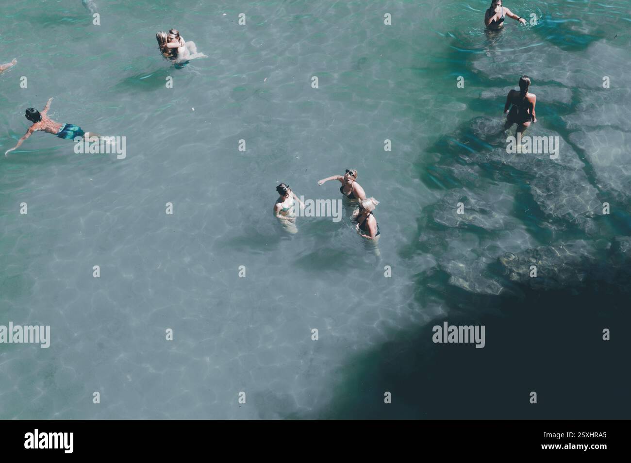 Swimmers float and chat in the clear green waters of Santa Marta beach, enjoying a peaceful ...