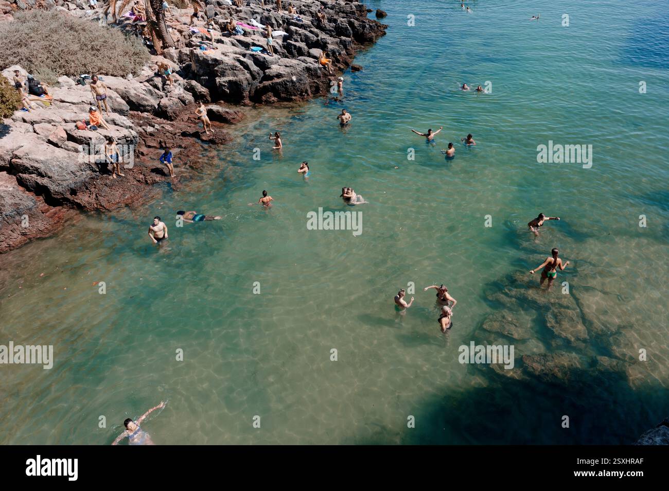 Swimmers enjoy the crystal-clear waters of Santa Marta beach, surrounded by rocky shores and ...