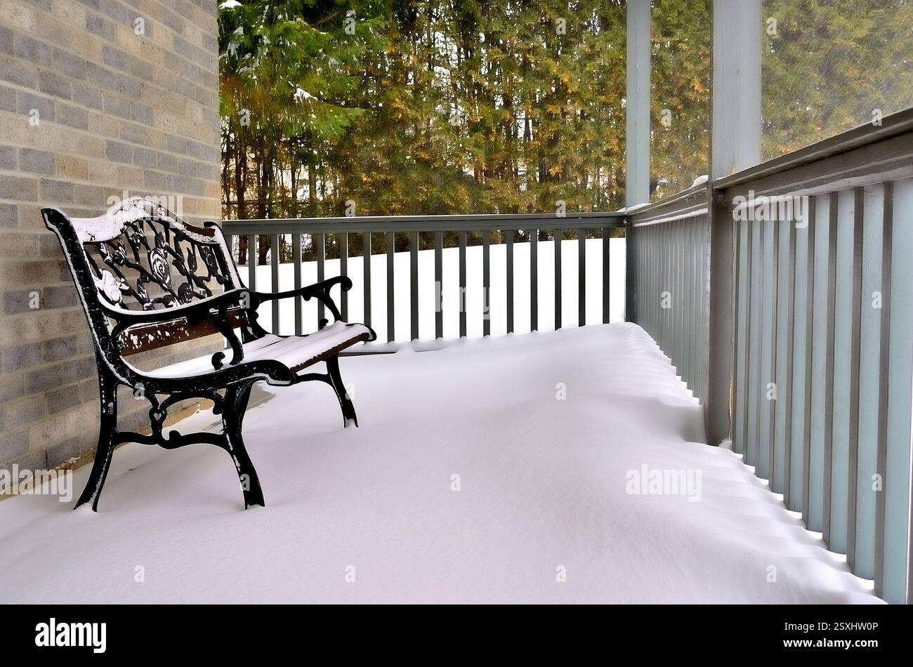 single cast iron park bench on a snow covered porch against a gray ...