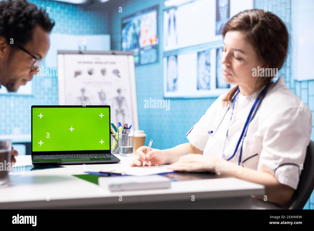 General practitioner and patient looking at green screen on device ...