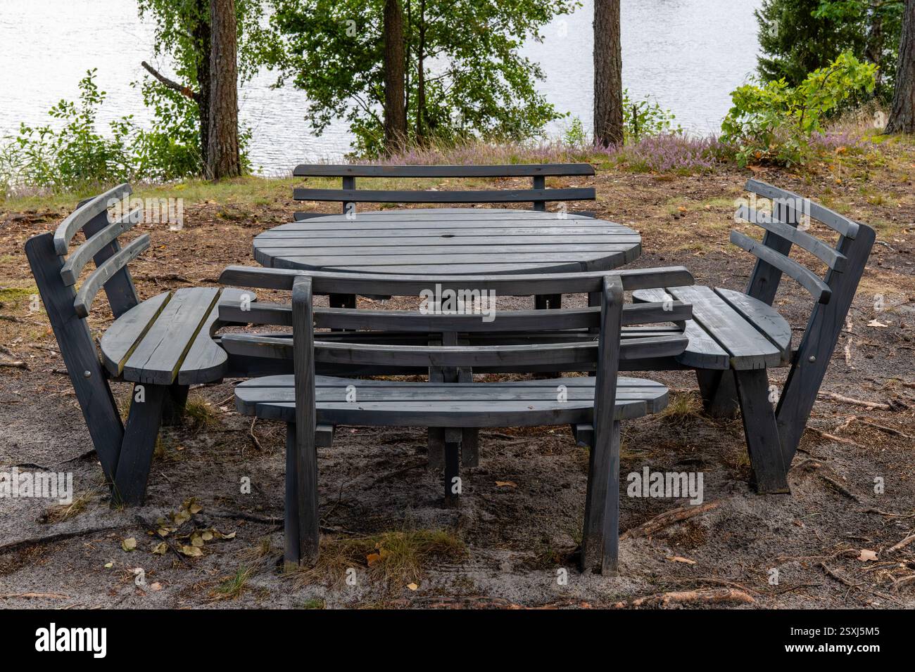 A grey circular picnic table with tourist benches by the lake in the ...