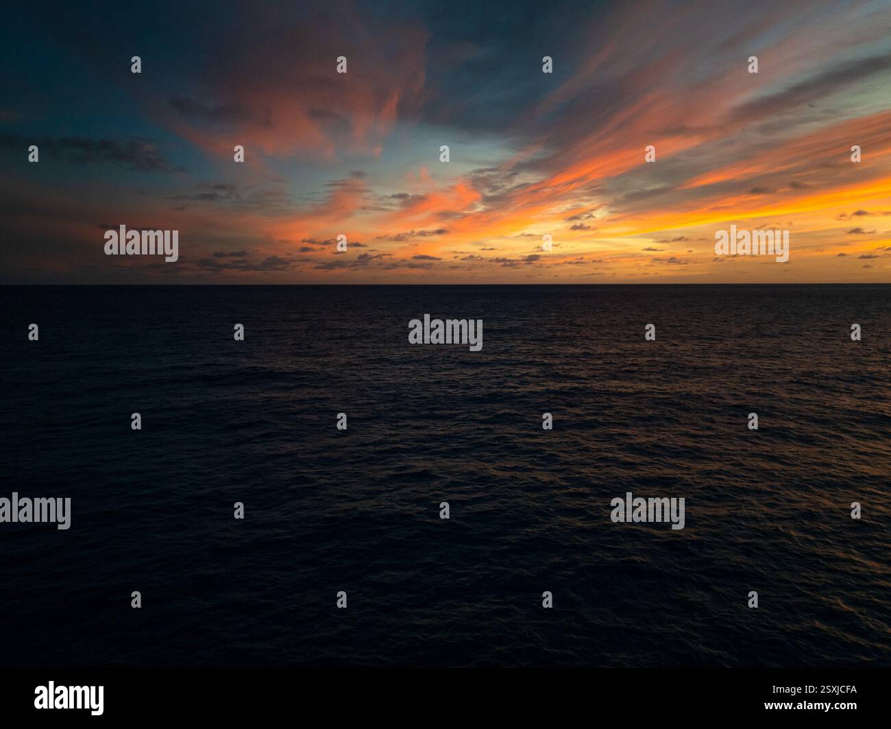 Dark ocean waves under a sky with orange and pink sunset clouds ...