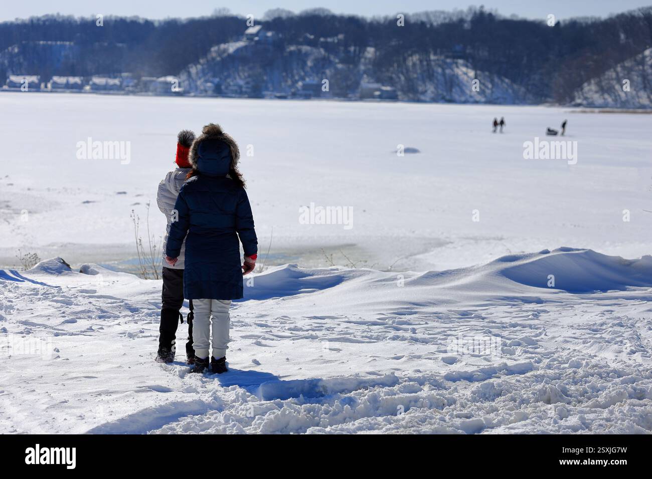 Two girls watching ice fishermen pull their sled across the ice Stock ...