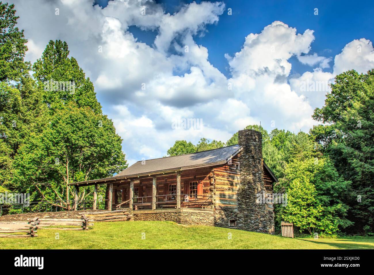 Log cabin with a stone chimney sits in a grassy field. The cabin is ...