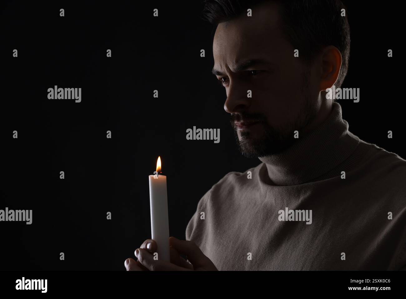 Sad man with burning candle crying on black background, space for text ...