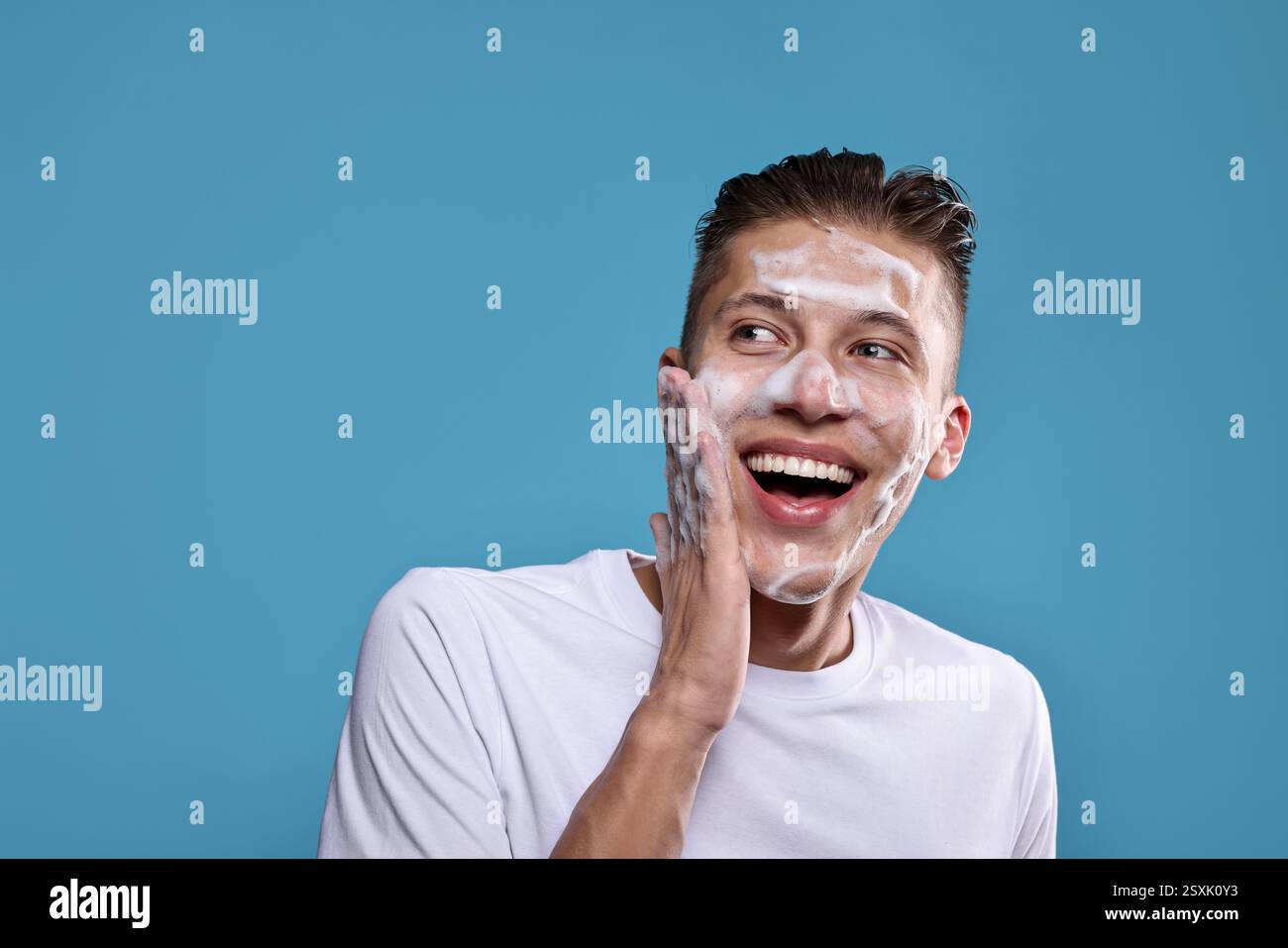 Smiling man washing his face with cleansing foam on blue background Stock Photo - Alamy