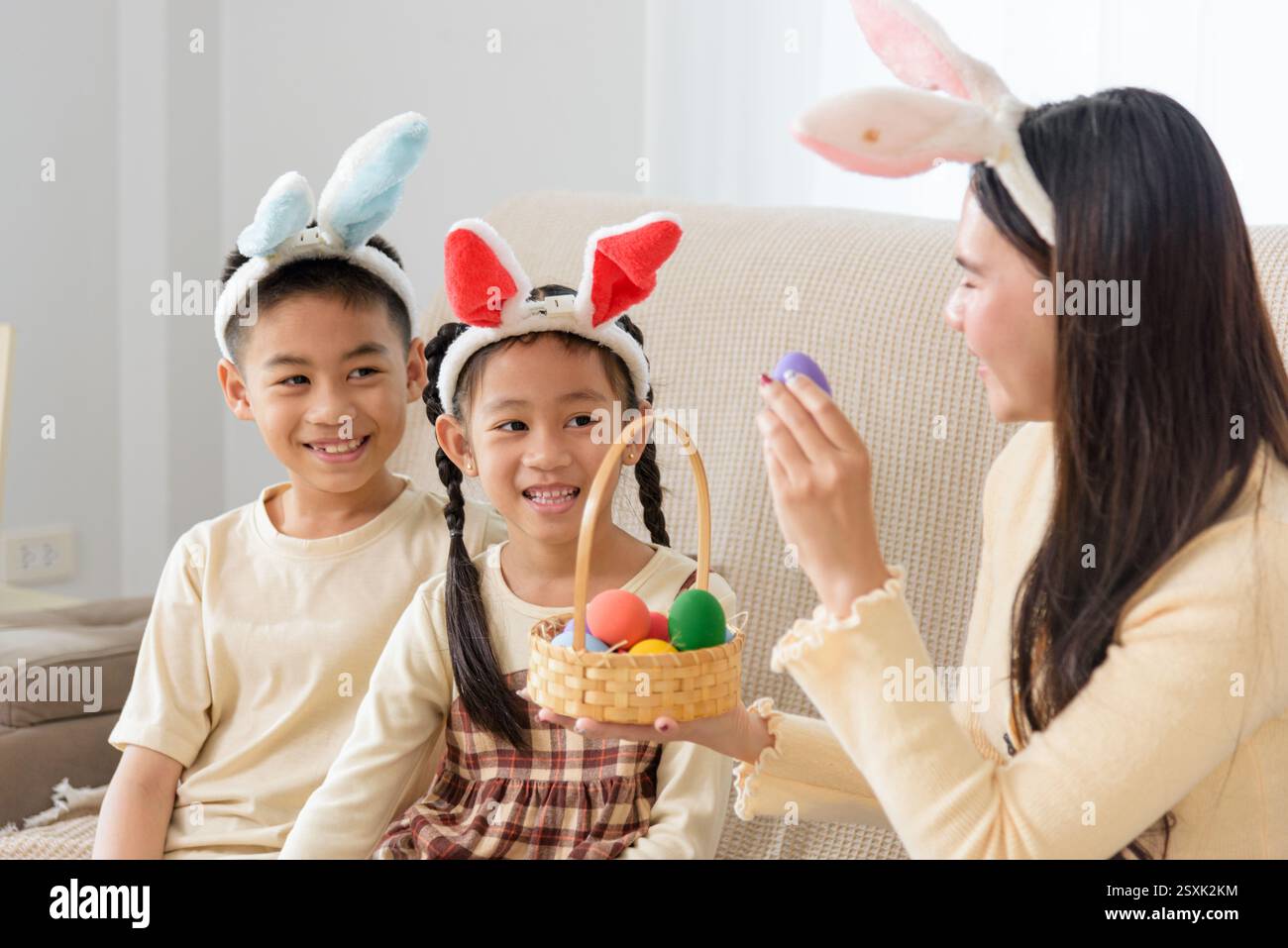 Easter egg hunt fun. A mother and children with bunny ears hold a festive basket of Easter eggs ...