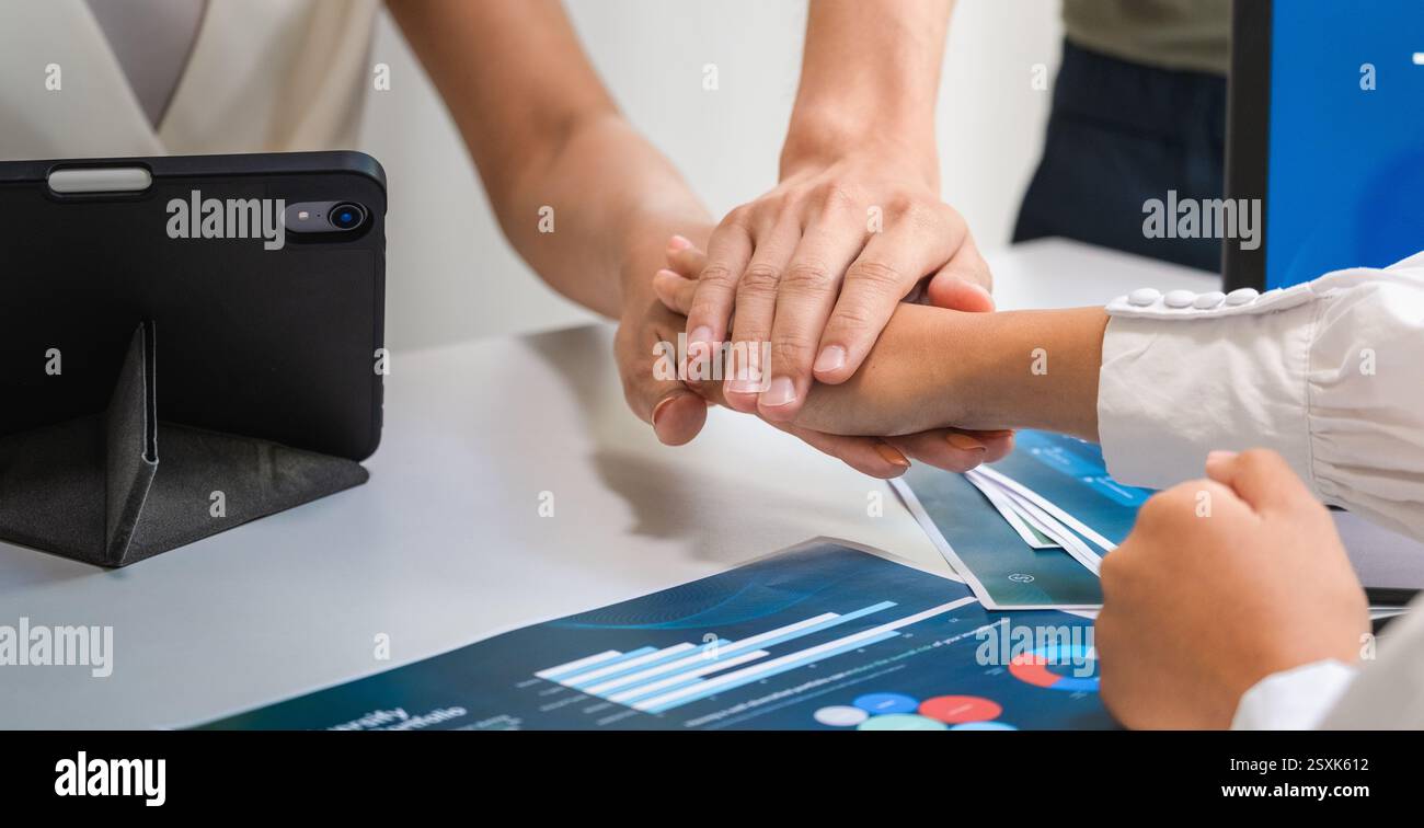 Close up team showing unity and support by stacking hands together in a ...