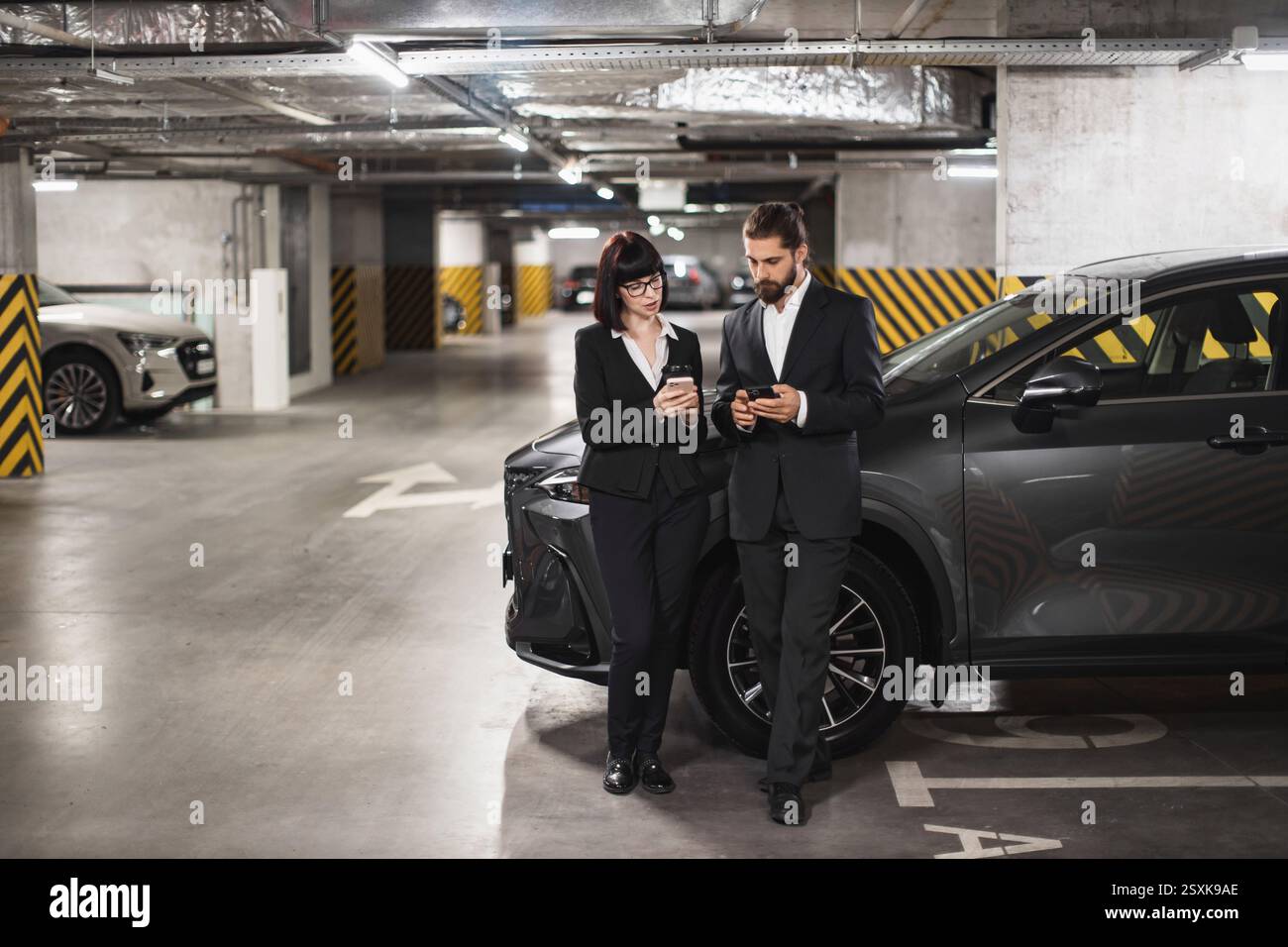 Caucasian man and woman standing by car in parking garage using ...