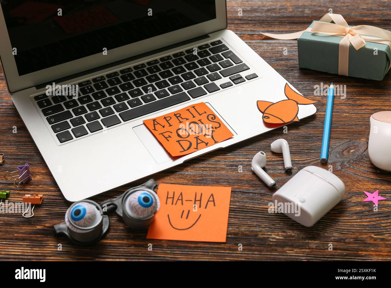 Laptop, funny glasses, gift box, earphones and sticky notes on wooden ...