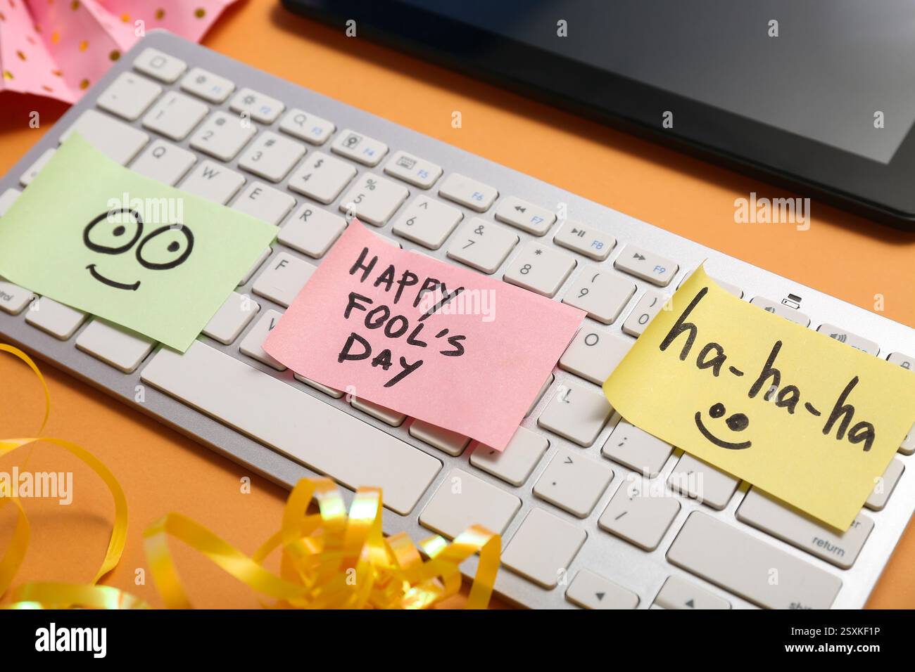 Tablet, computer keyboard and sticky notes on orange background. April ...