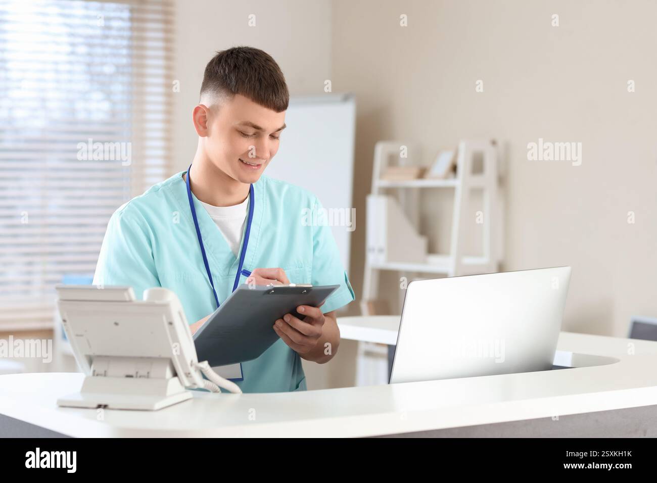 Male medical intern writing on clipboard at reception desk in clinic ...