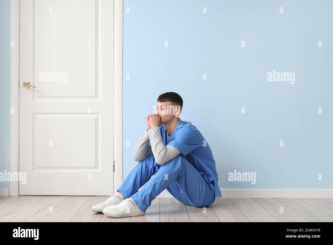 Stressed male medical intern sitting near blue wall Stock Photo - Alamy
