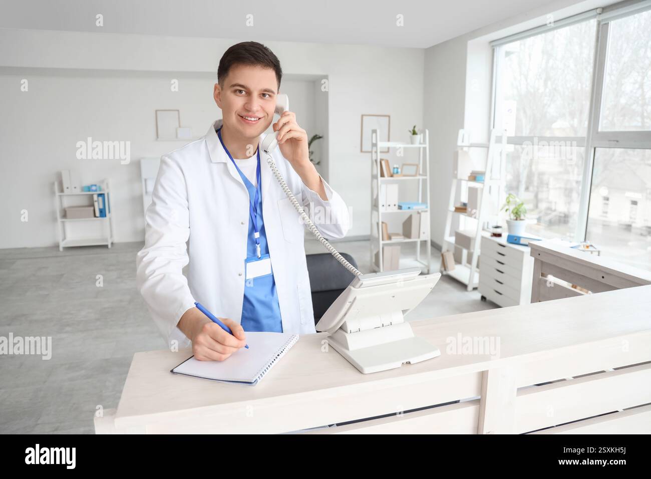 Male medical intern talking by telephone at reception desk in clinic ...