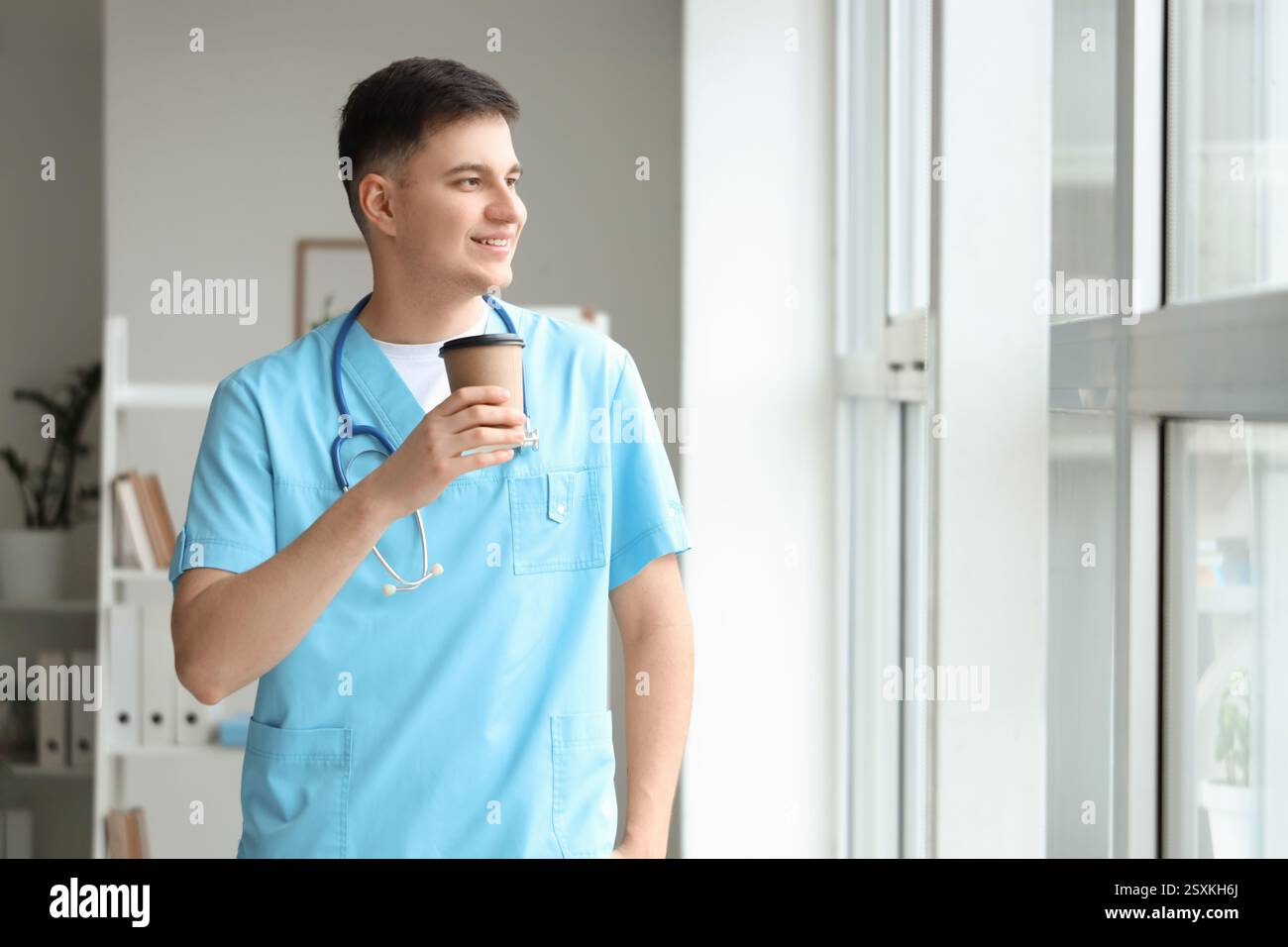 Male medical intern with coffee cup near window in clinic Stock Photo ...