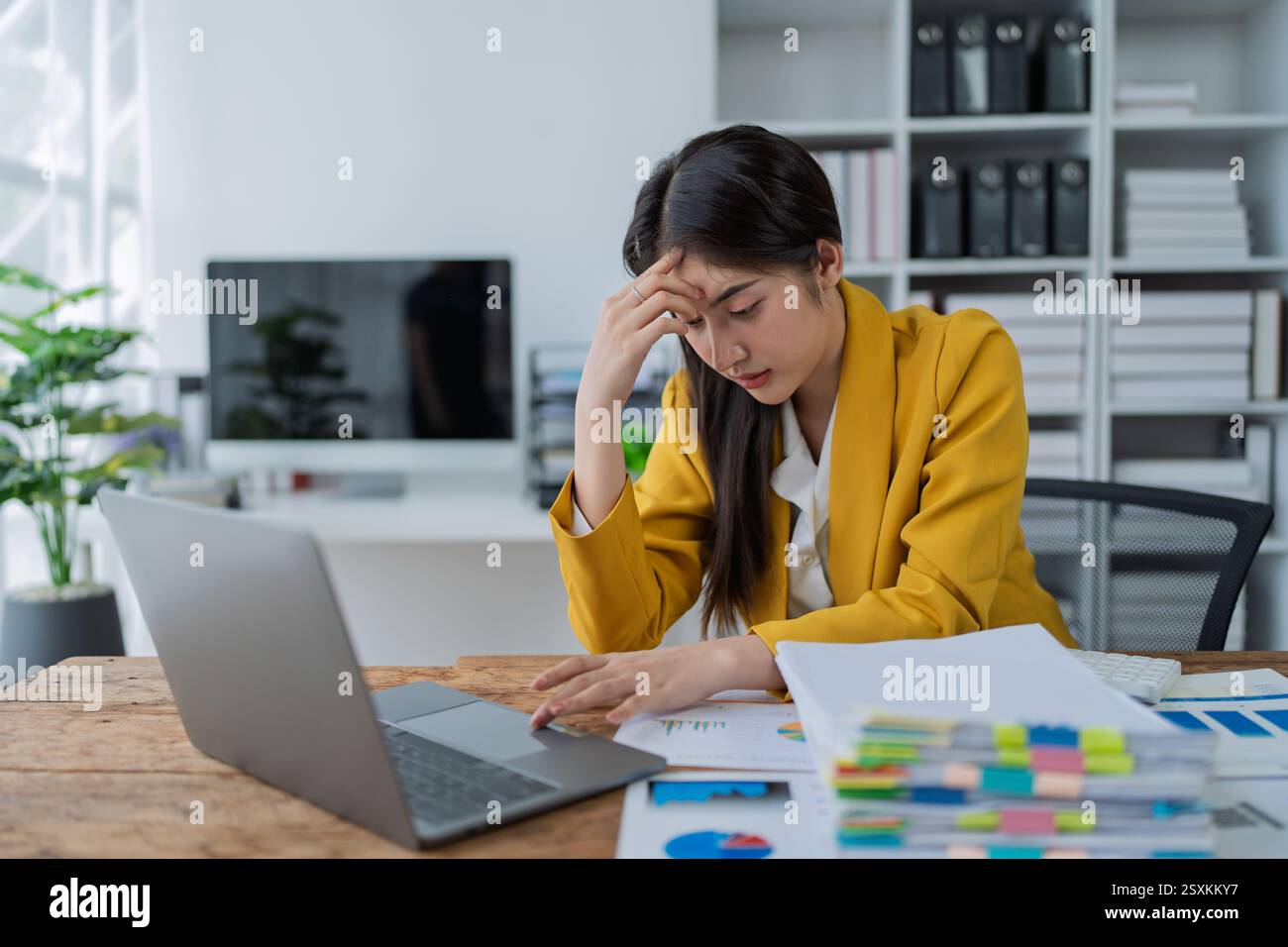 Stressed businesswoman in yellow blazer working on laptop surrounded by ...