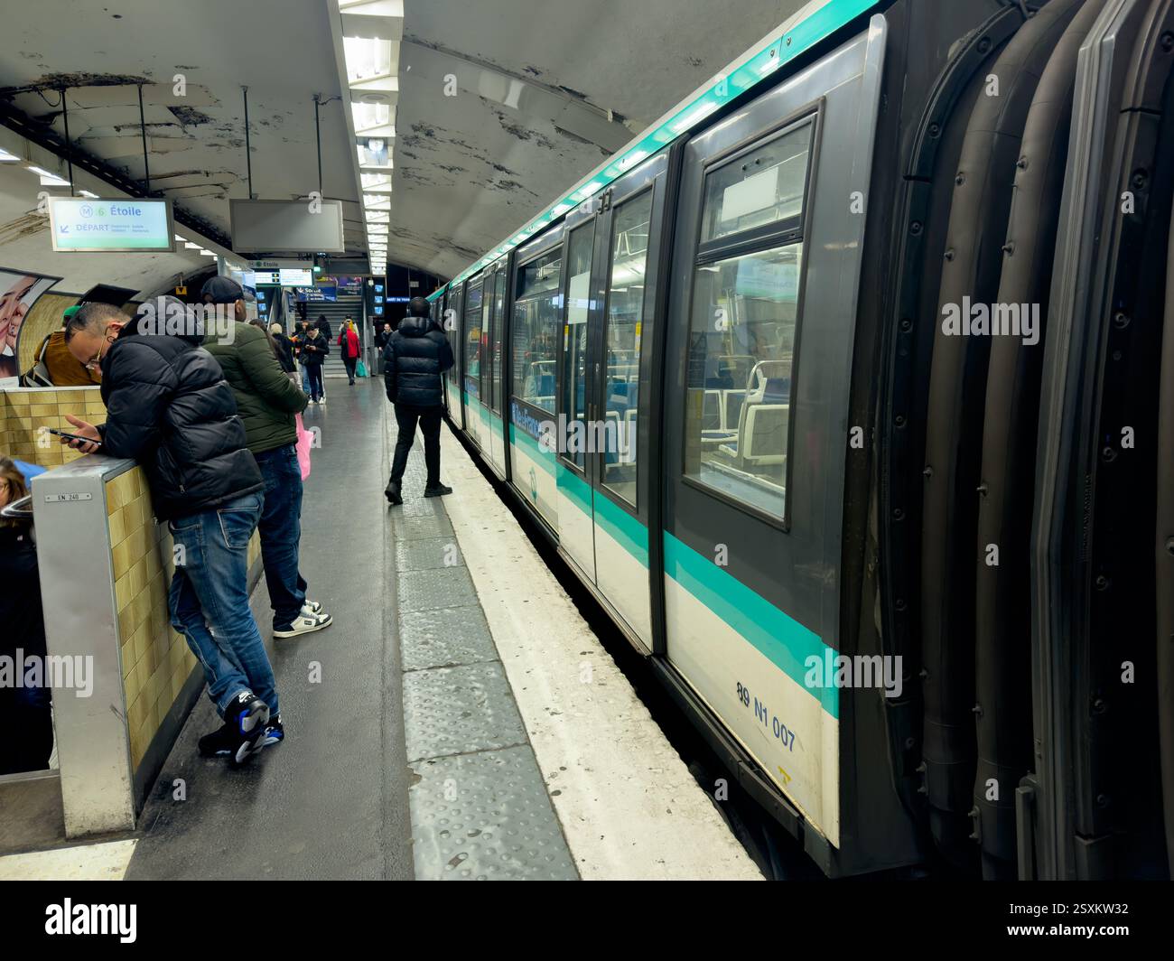 Commuters await the arriving train at a bustling urban metro station ...