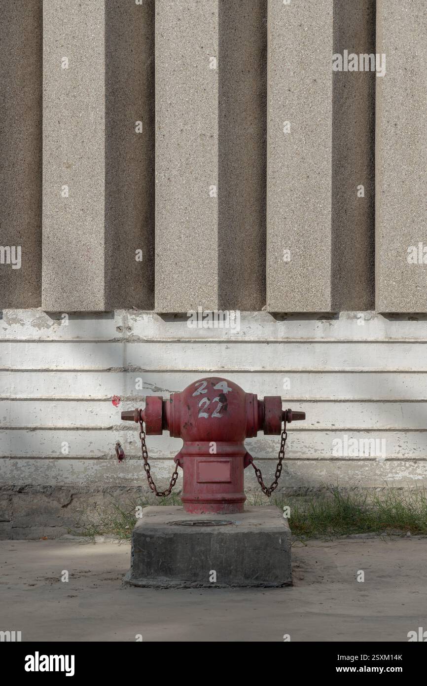 A old red fire hydrant with a chain stand on sidewalk in front of wall ...
