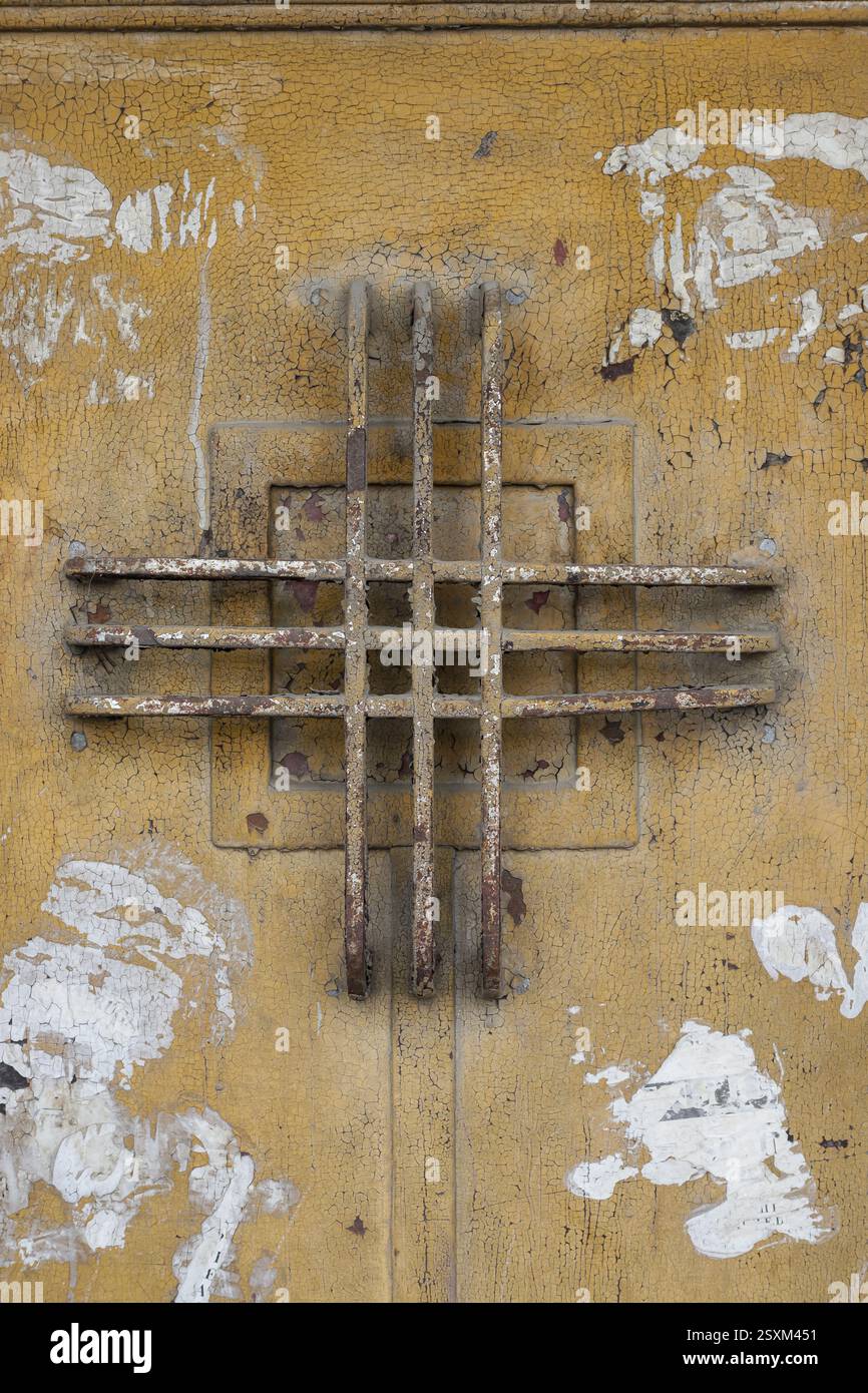 A weathered yellow wall features a rusty metal grid pattern, revealing ...